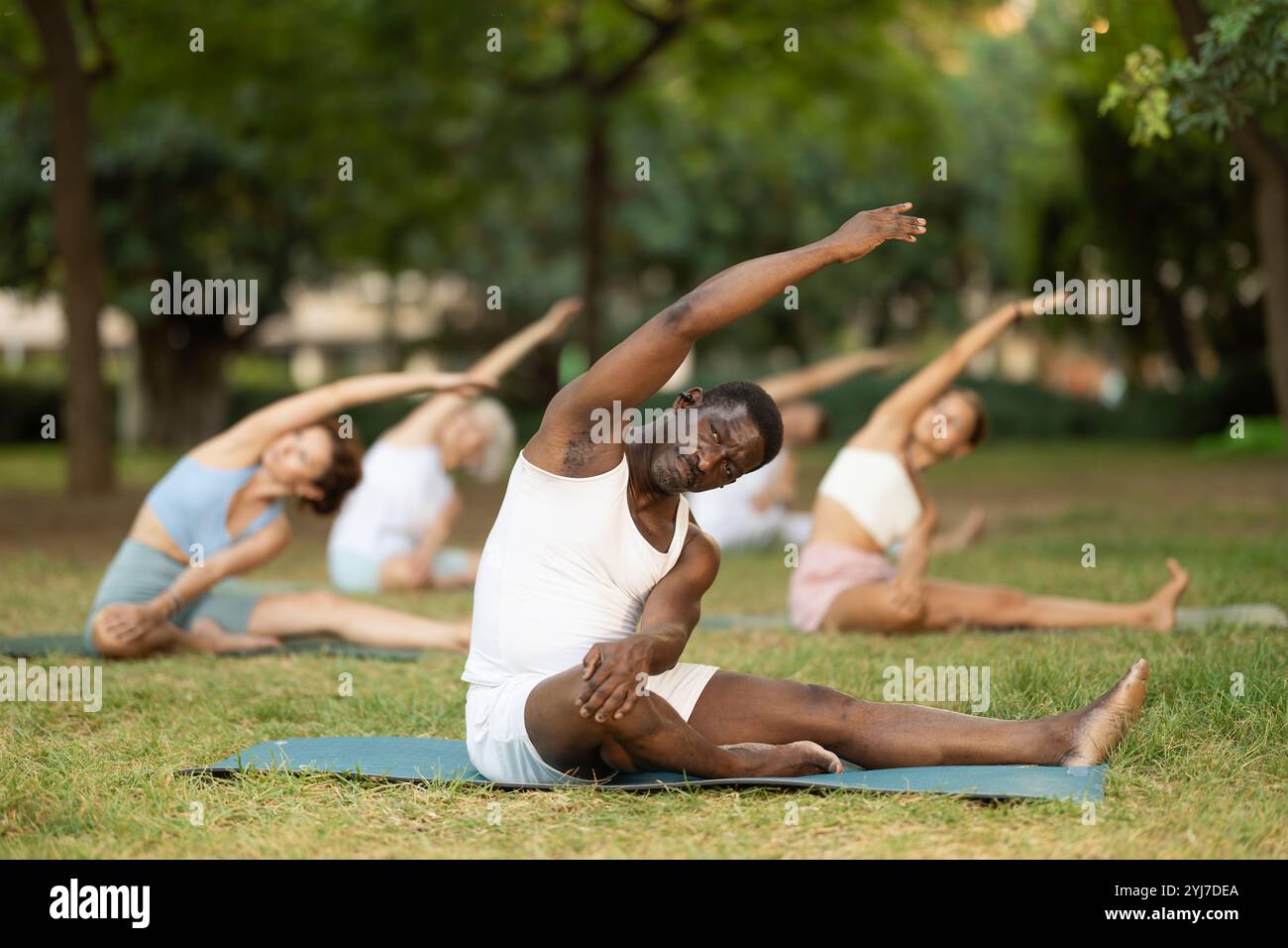 African american man practices yoga in summer park with other athletes ...