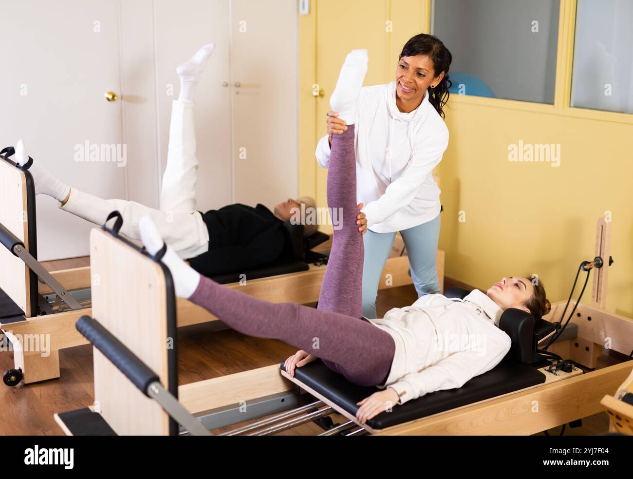 Hispanic female pilates instructor helping girl exercising on reformer ...