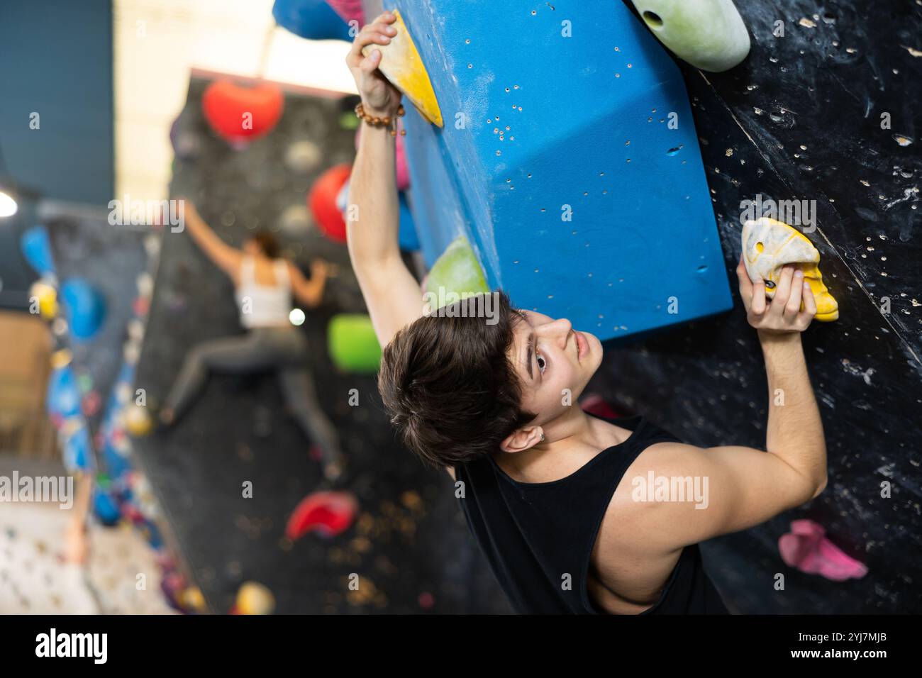 young muscular male sportsman climbing black wall for bouldering in gym ...