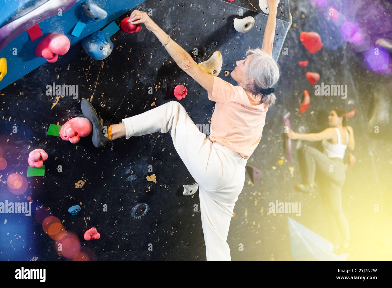 Mature female fitness climber training at bouldering gym.Woman rise up ...