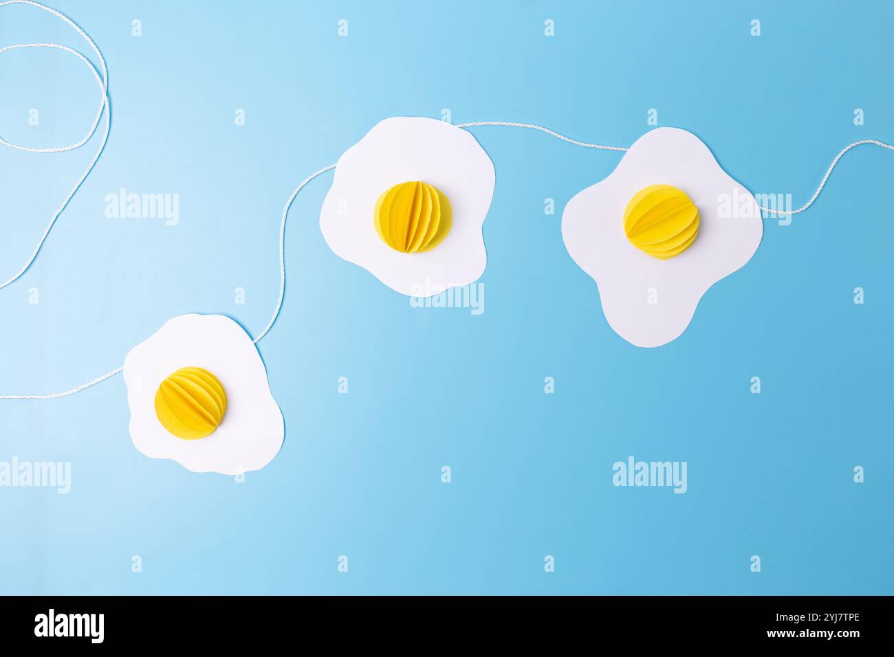 three fried eggs paper craft hanging from a string on a blue background ...