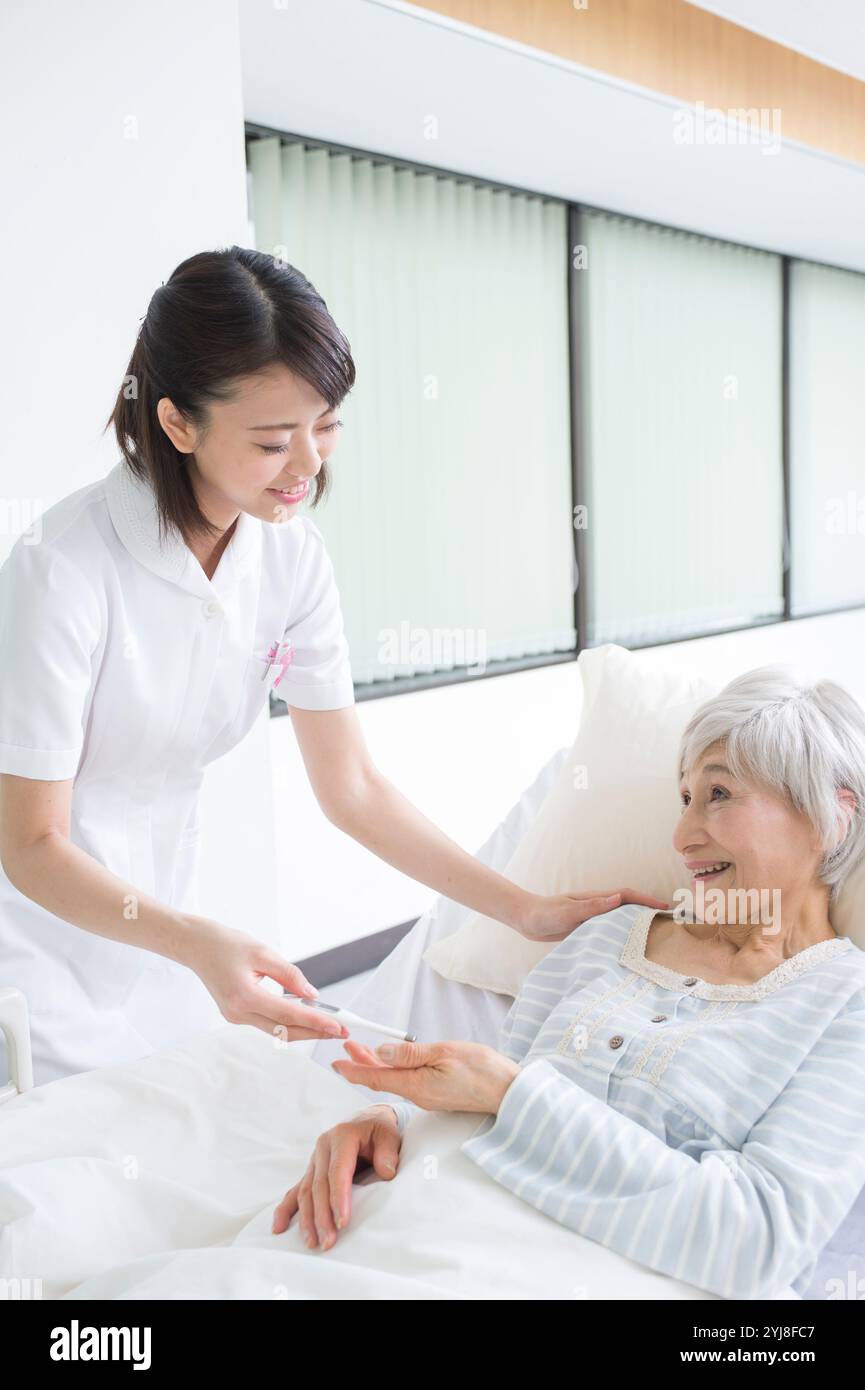 Nurse giving a thermometer to a hospitalised senior female patient in ...