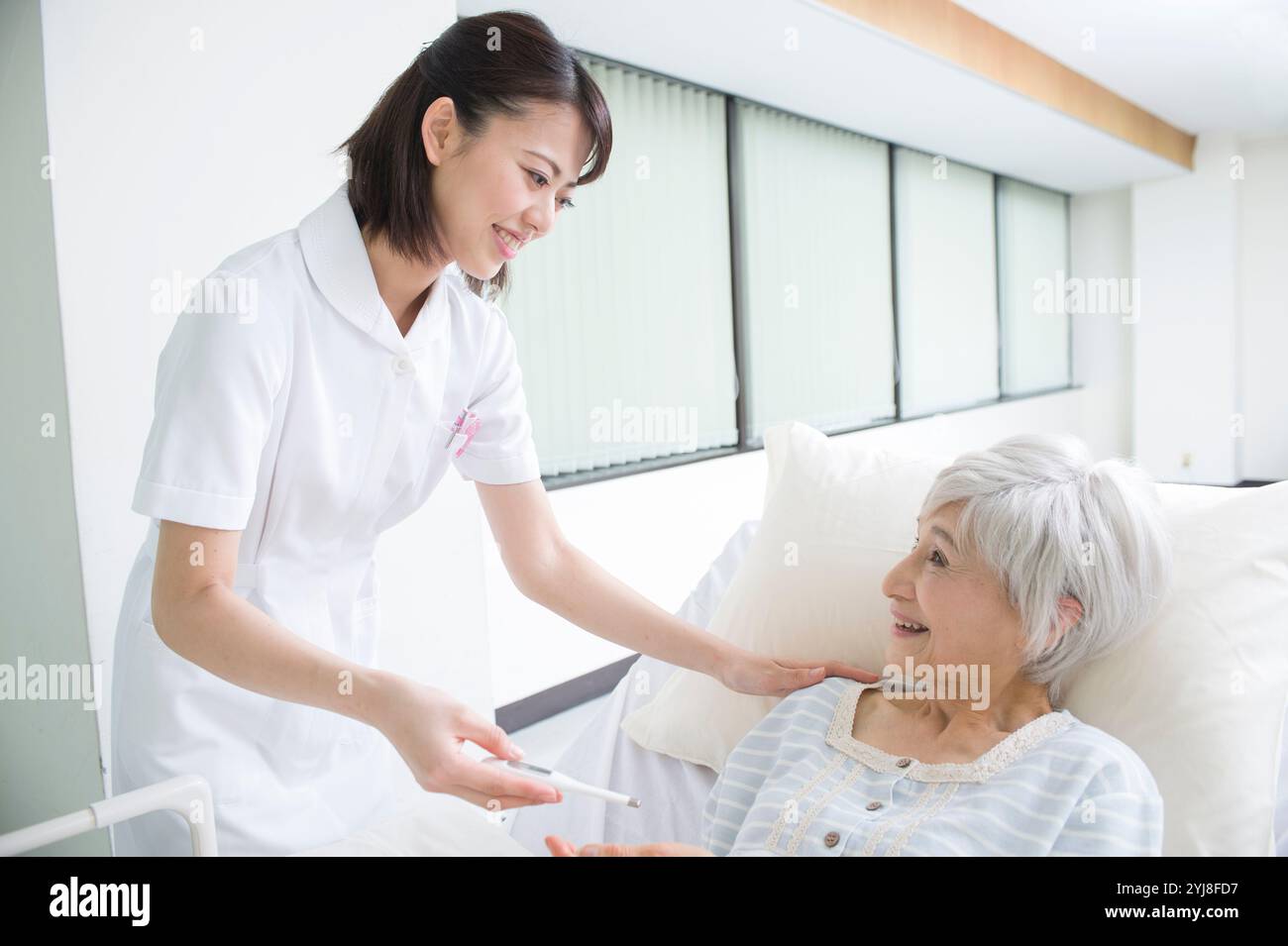 Nurse giving a thermometer to a hospitalised senior female patient in ...