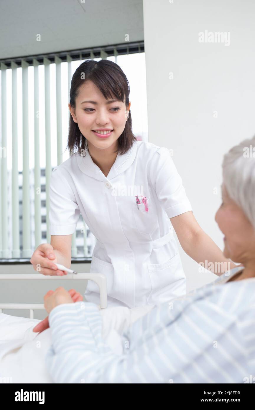 Nurse giving a thermometer to a hospitalised senior female patient in ...