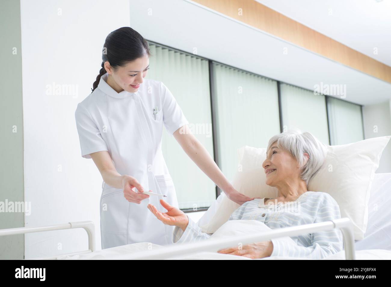 Nurse giving a thermometer to a hospitalised senior female patient in ...