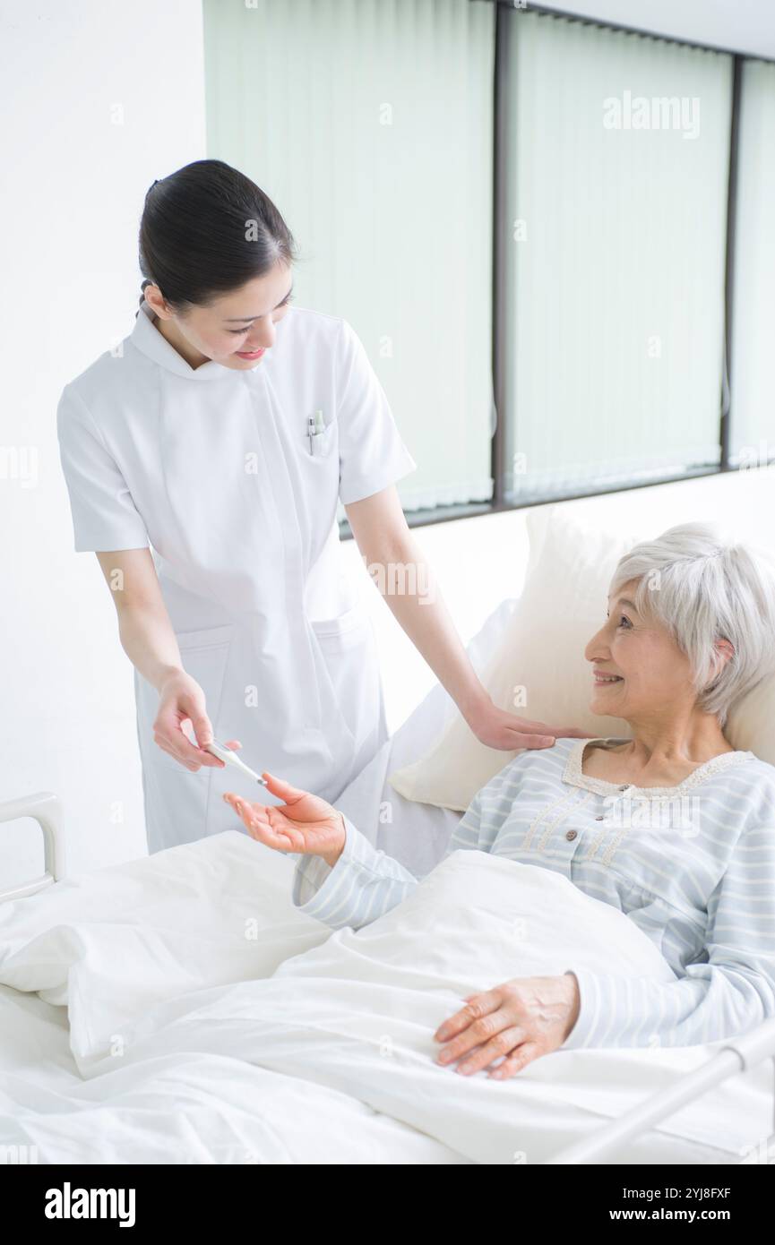 Nurse giving a thermometer to a hospitalised senior female patient in ...
