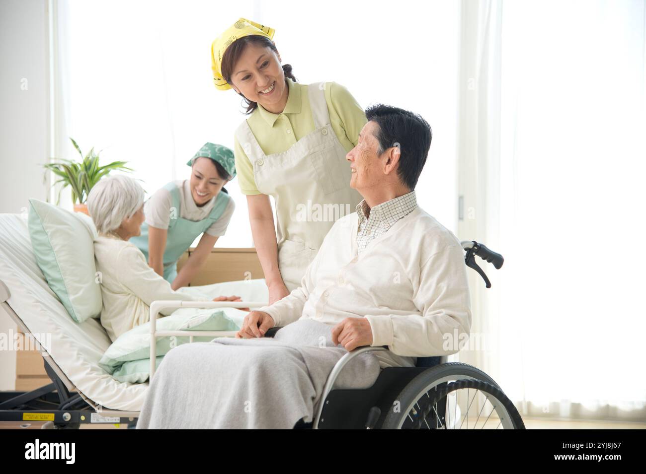 Caregiver helper with elderly person in care bed and wheelchair Stock ...