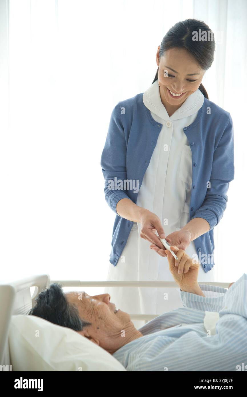 Nurse giving thermometer to hospital-bed old man Stock Photo - Alamy
