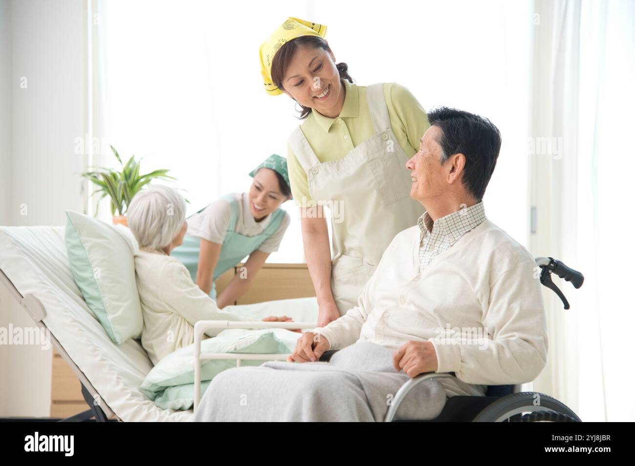 Caregiver helper with elderly person in care bed and wheelchair Stock ...