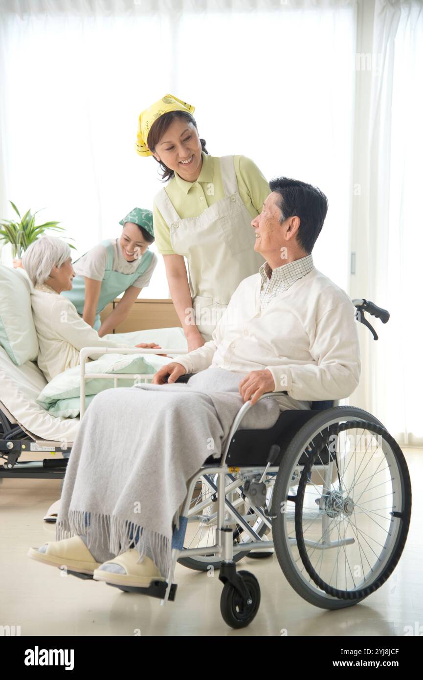 Caregiver helper with elderly person in care bed and wheelchair Stock ...