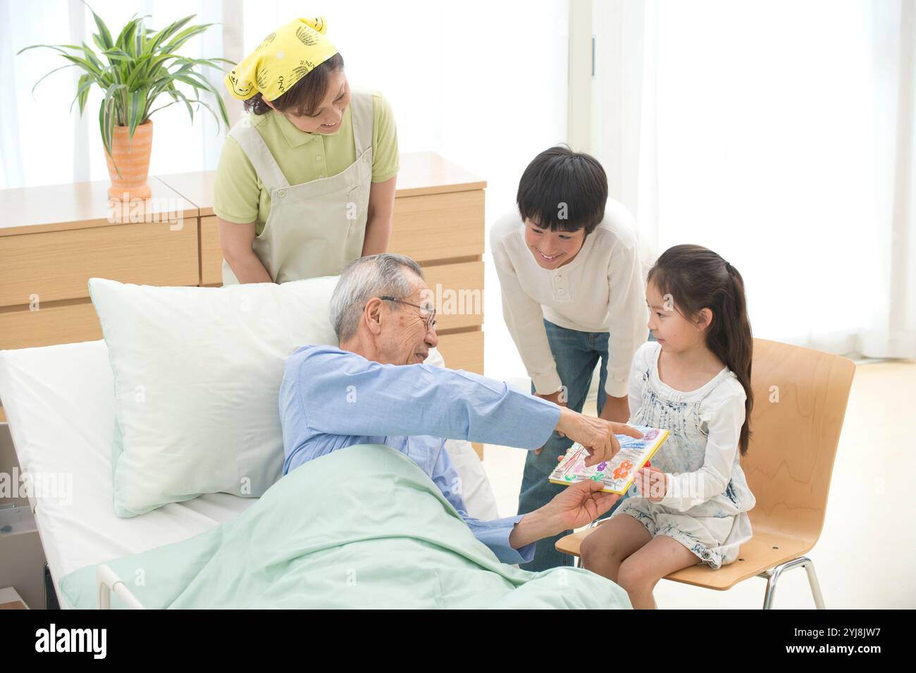 Care helper with elderly person in care bed and grandson showing him a ...