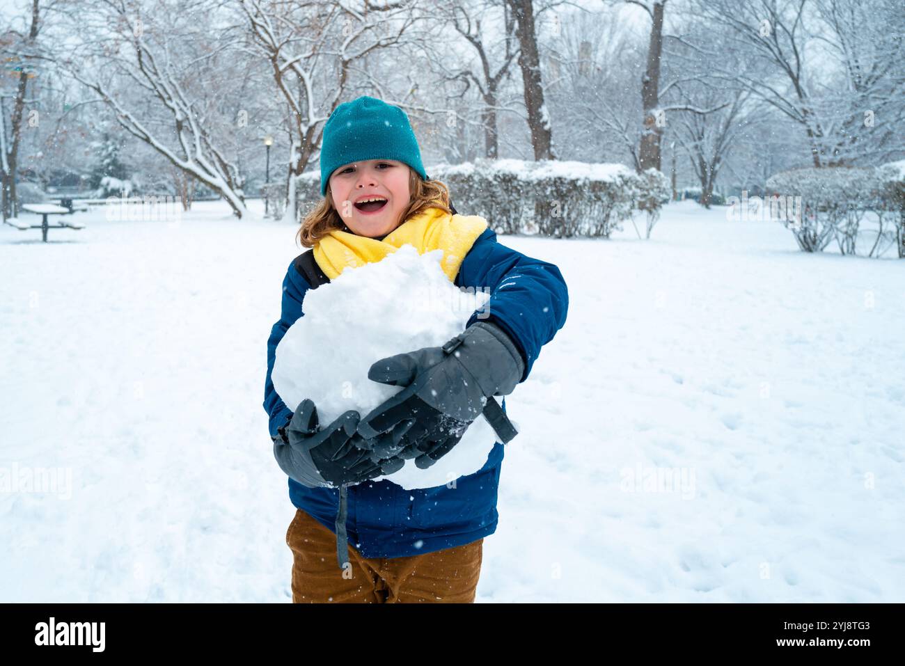 Happy Kid in winter park on a snowy cold winter day. Cute child playing ...