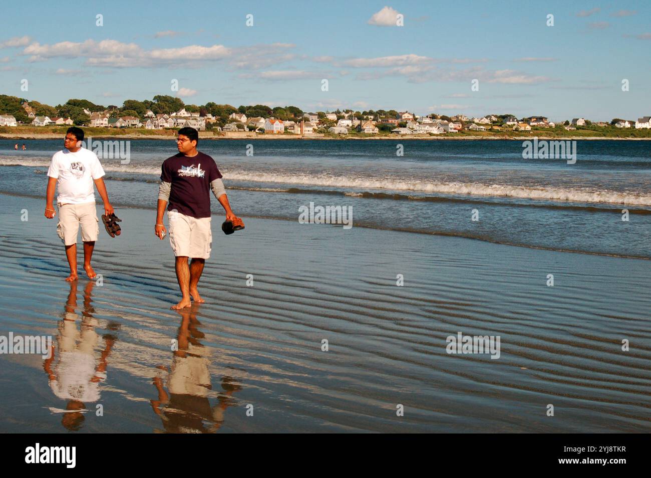 Two male friends wade in the shallow water at low tide on a beach in ...