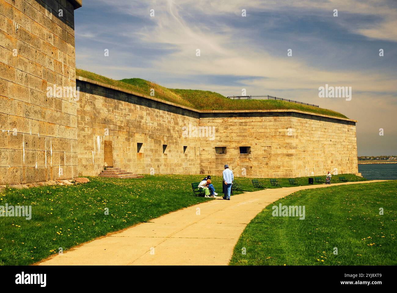 People enjoy relaxing on a park bench near the imposing stone fortress ...