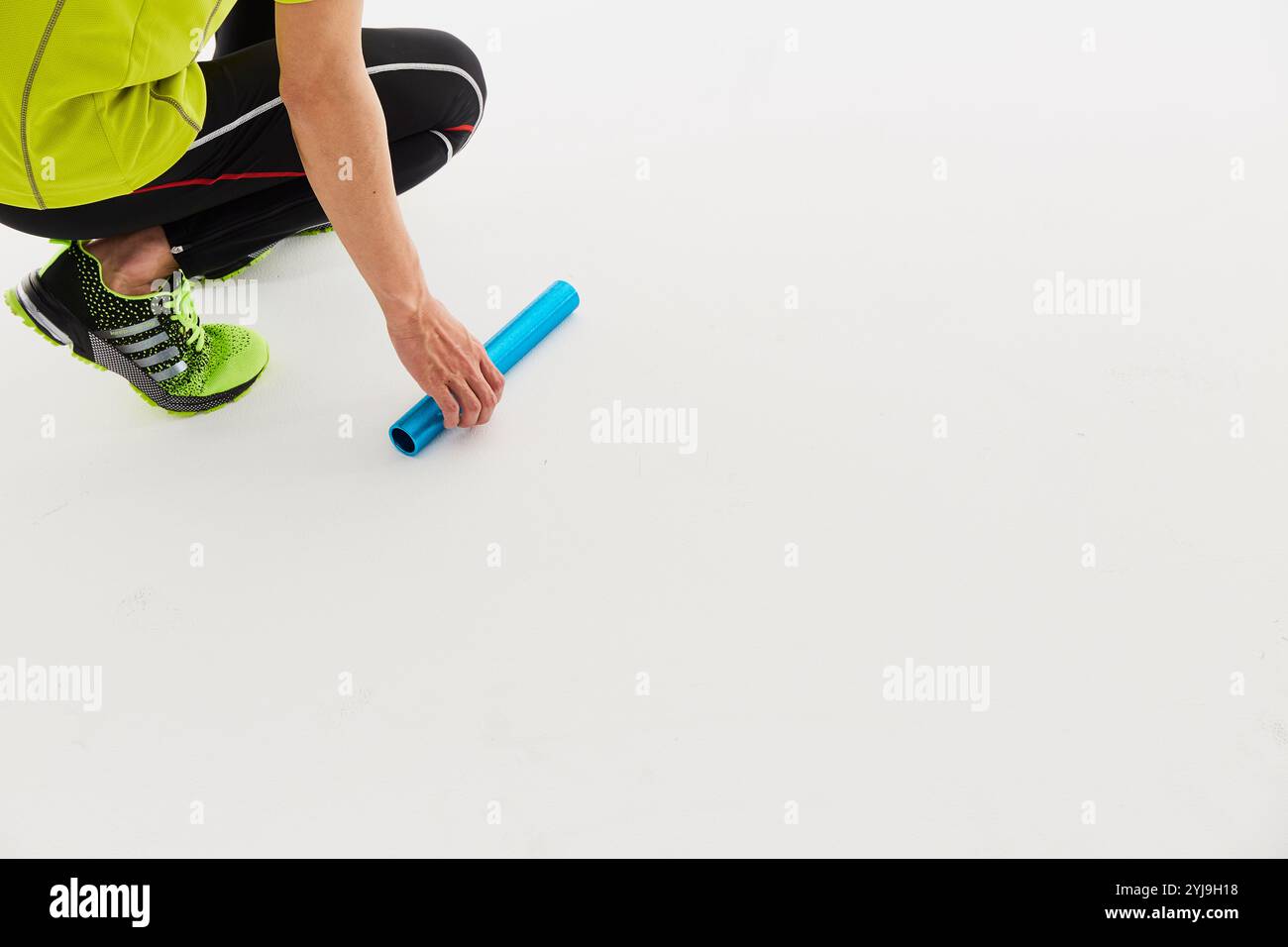 Male track and field athlete with relay baton in starting position ...