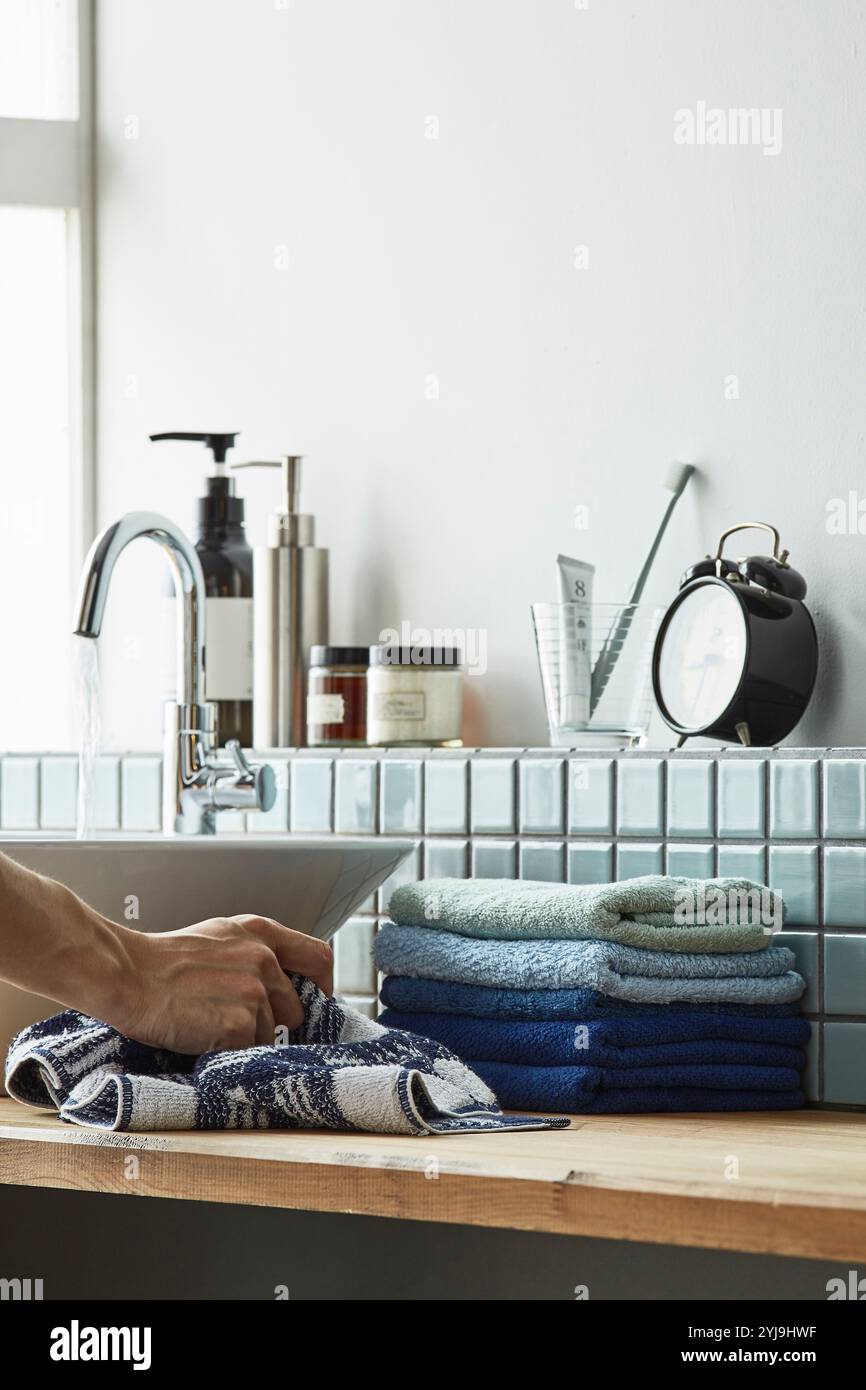 White wall and light blue tile washbasin and man's hand grabbing towel ...