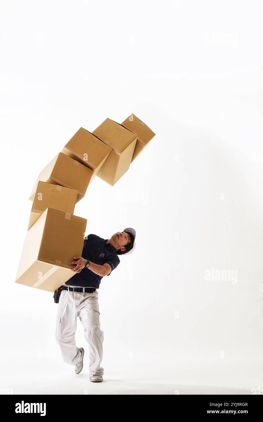 Man in work clothes carrying many stacks of cardboard boxes in white ...