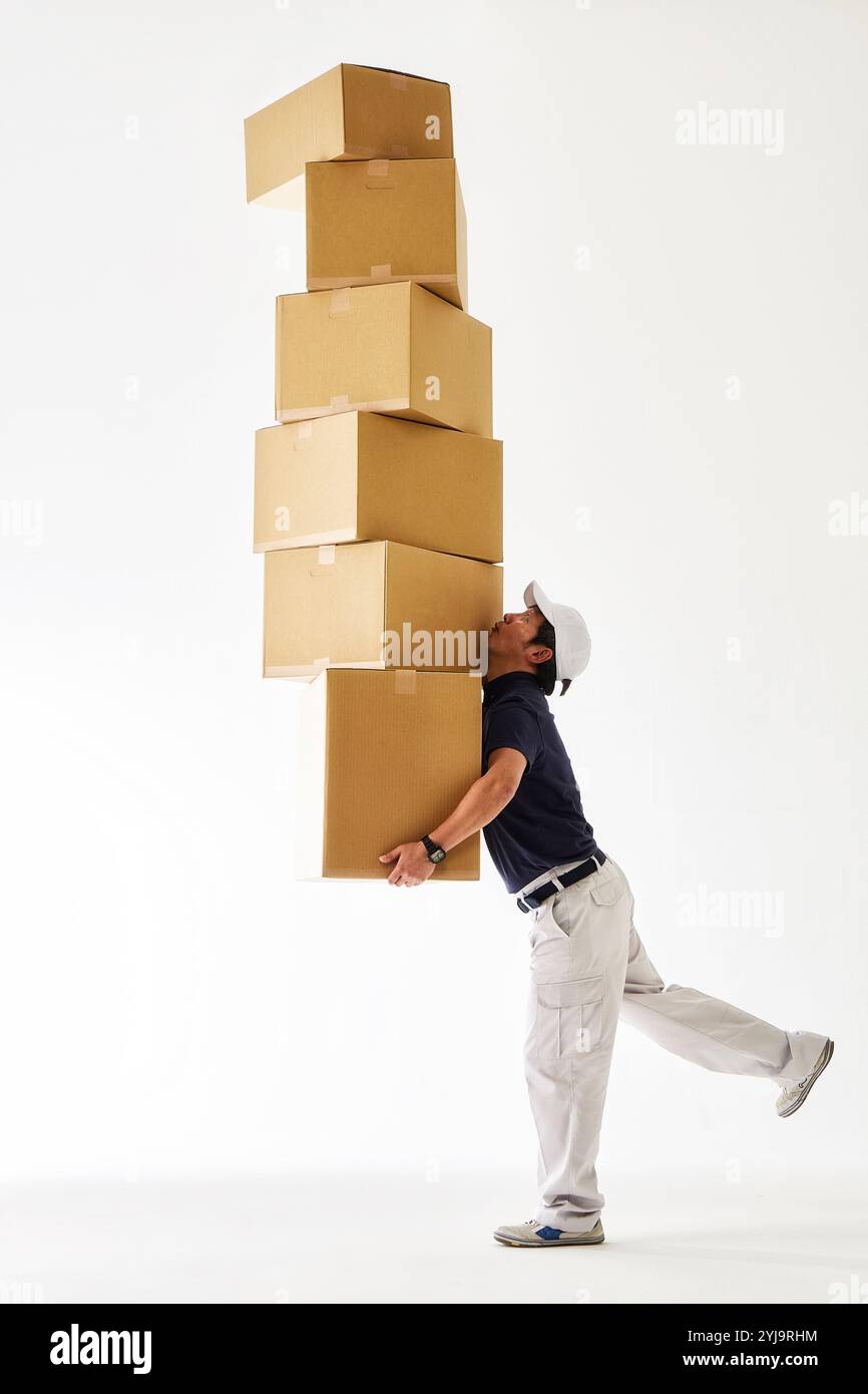 Man in work clothes carrying many stacks of cardboard boxes in white ...