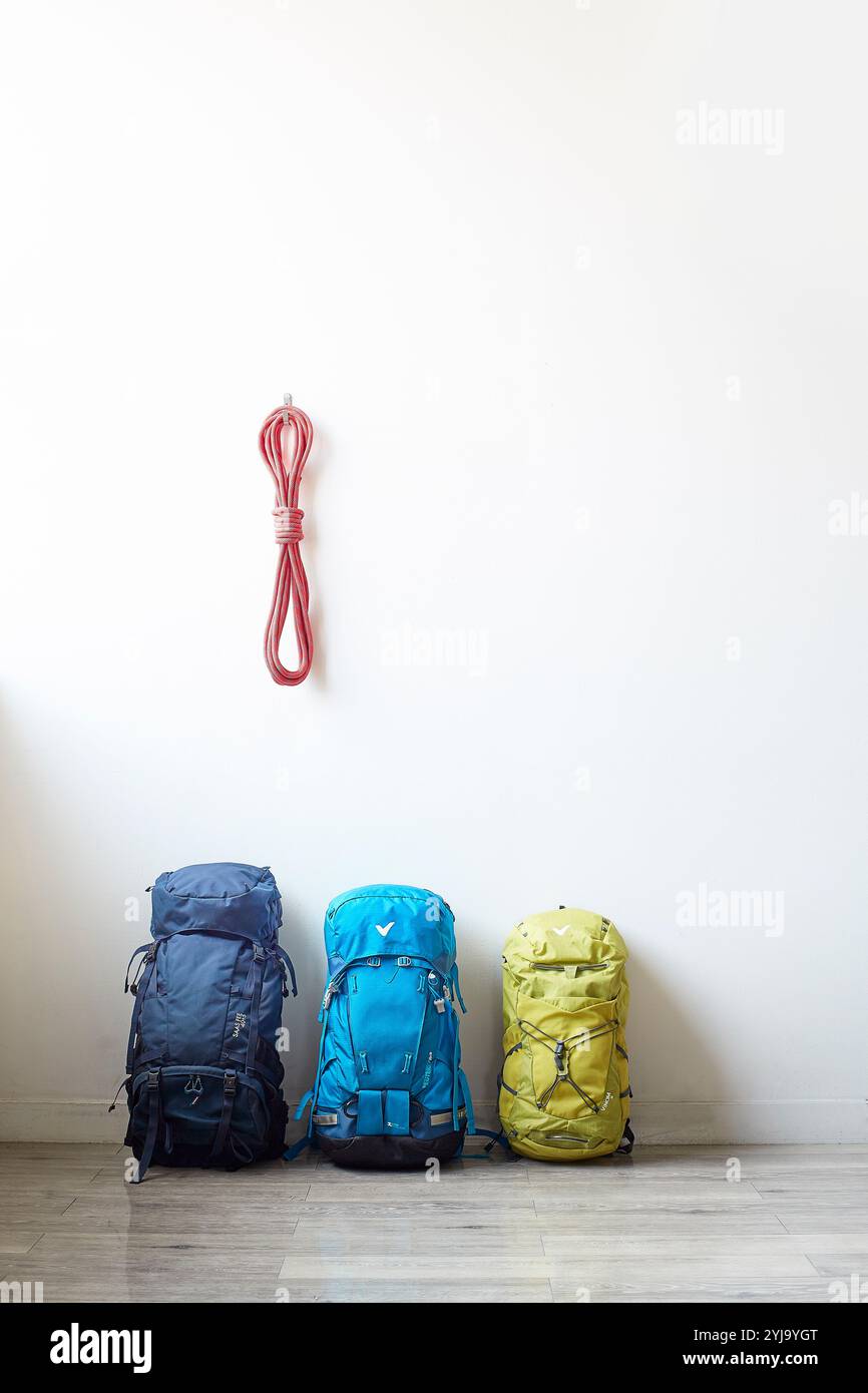 Climbing rope hanging on the white wall and three rucksacks of ...