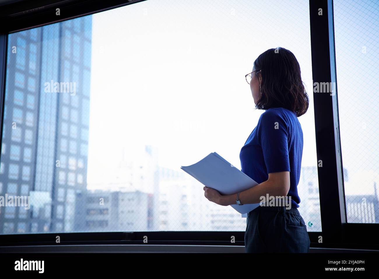 Woman holding papers and staring out window Stock Photo - Alamy