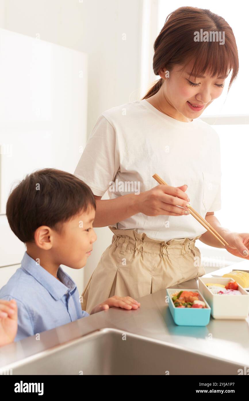Woman making lunch in the kitchen with a boy cuddling with her Stock ...