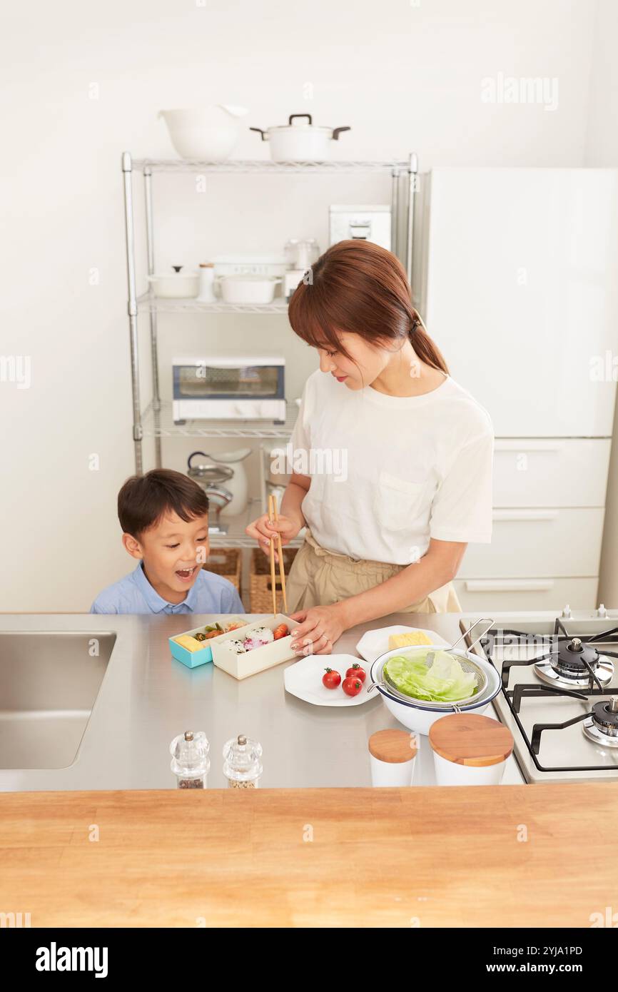 Woman making lunch in the kitchen with a boy cuddling with her Stock ...