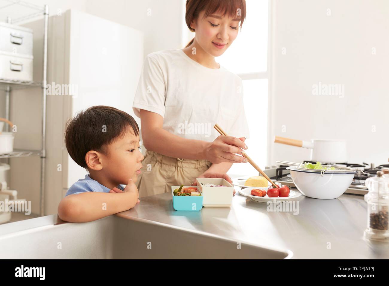 Woman making lunch in the kitchen with a boy cuddling with her Stock ...