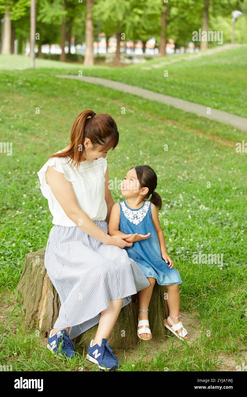 Mother and girl sitting next to each other on stumps in the park ...