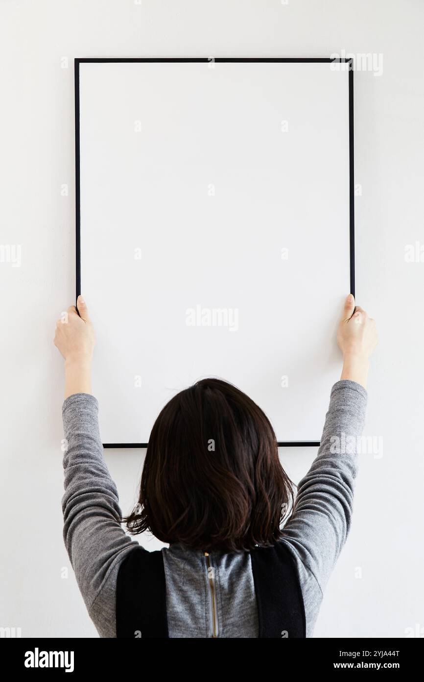 Woman hanging frame on wall Stock Photo - Alamy