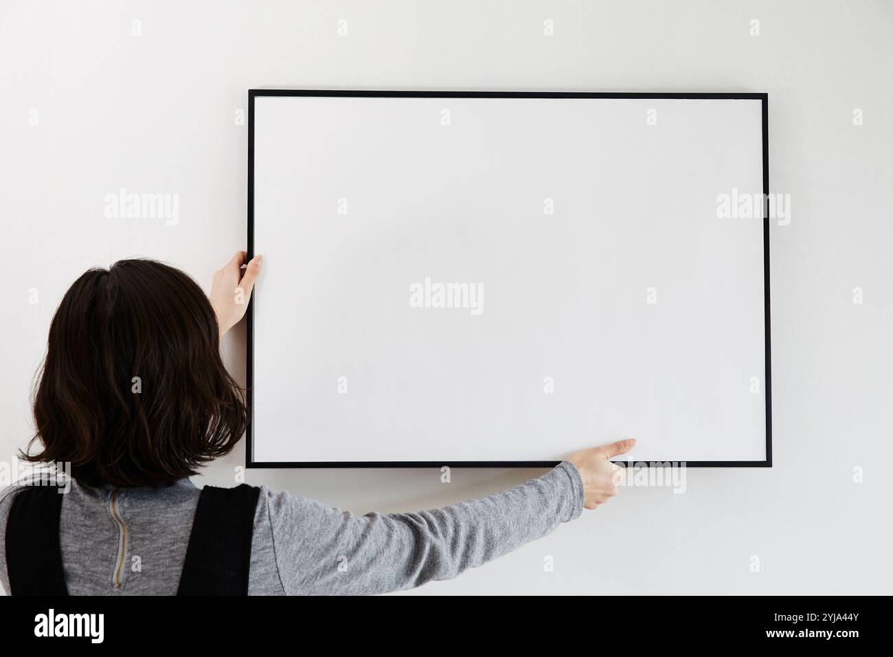 Woman hanging frame on wall Stock Photo - Alamy