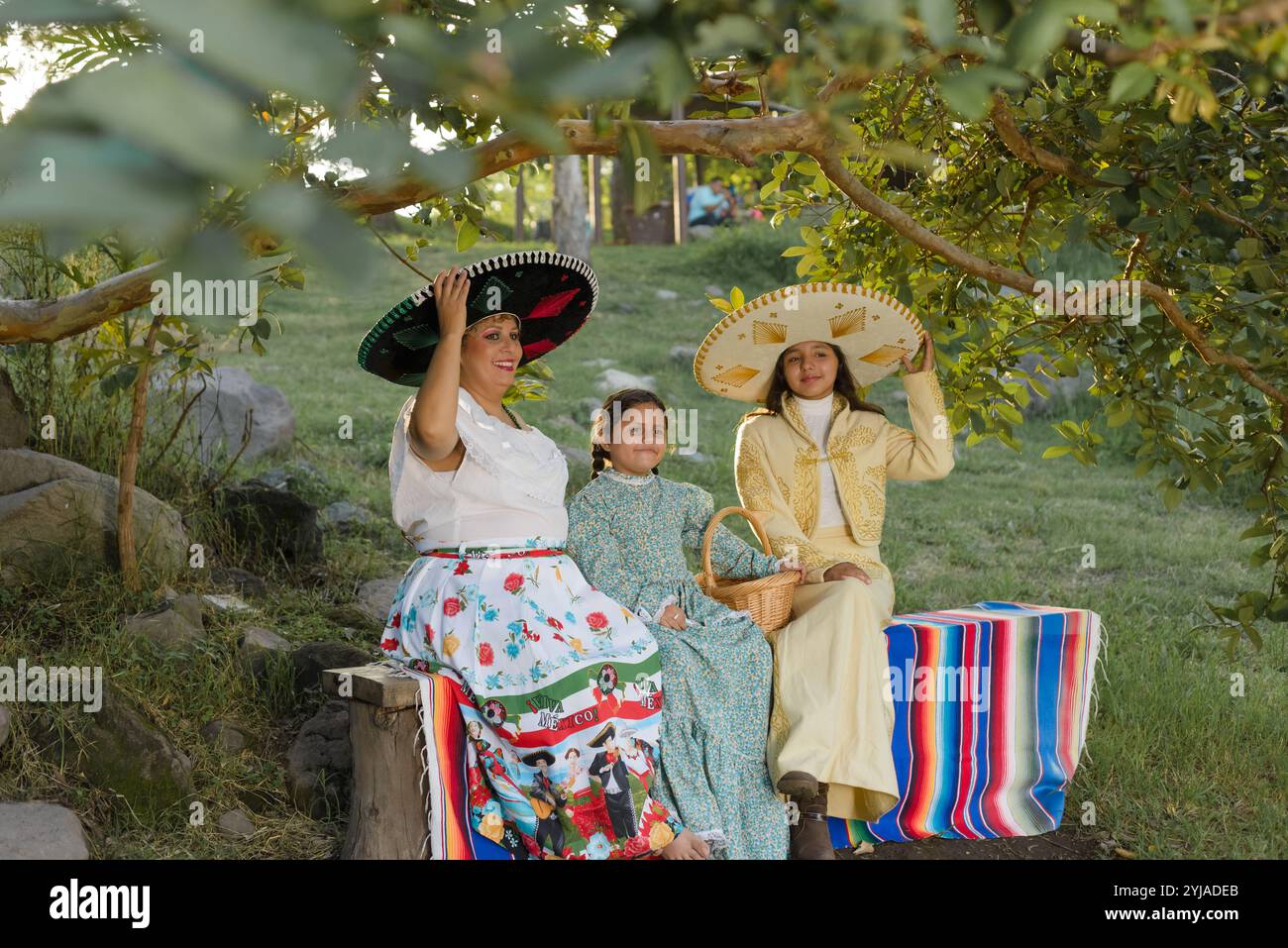 Mother with her daughters wearing typical mexican clothes sitting on sarapes. Rural scenery ...