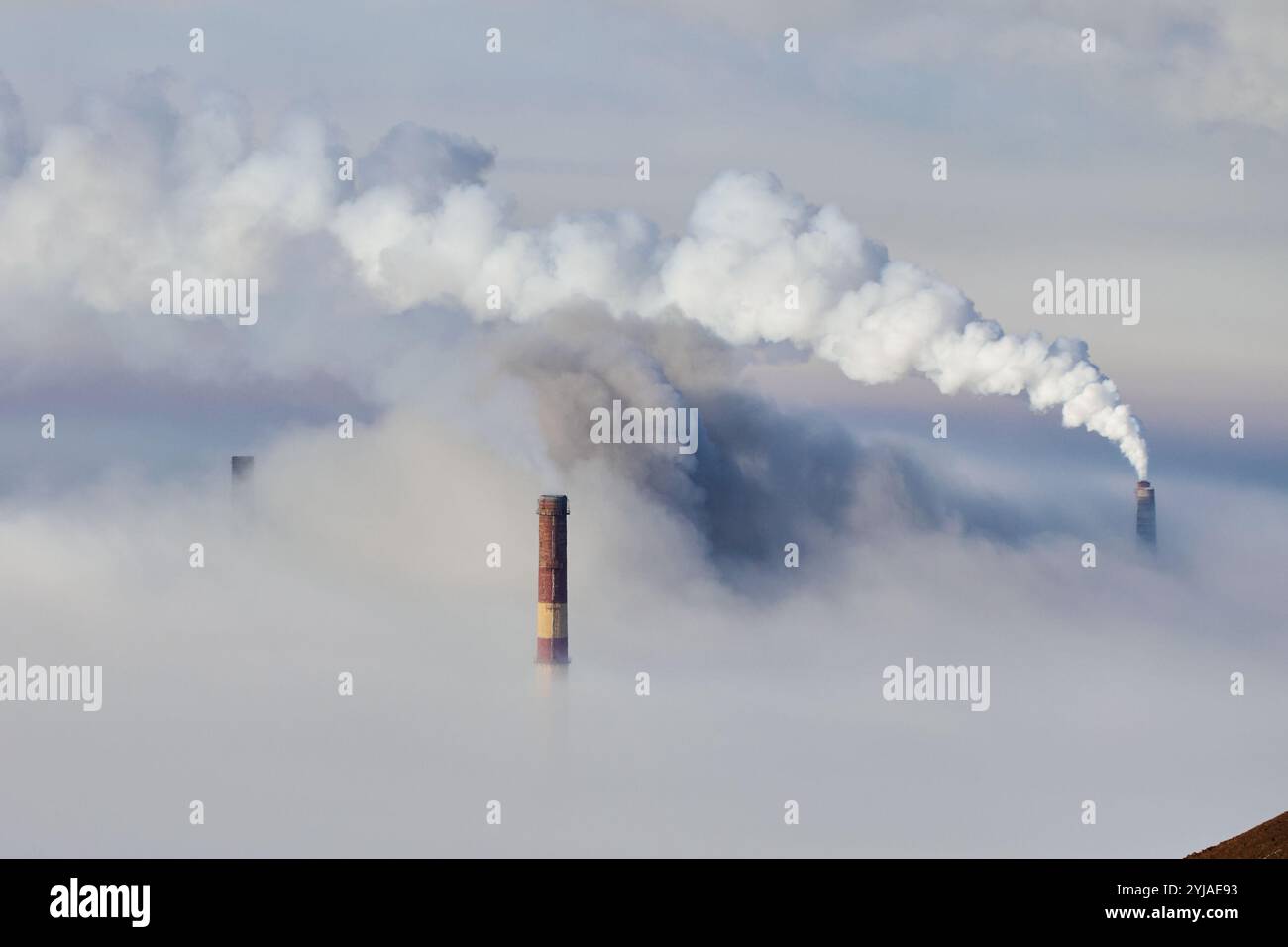 Smoke billows from industrial chimneys obscured by fog in a remote area ...