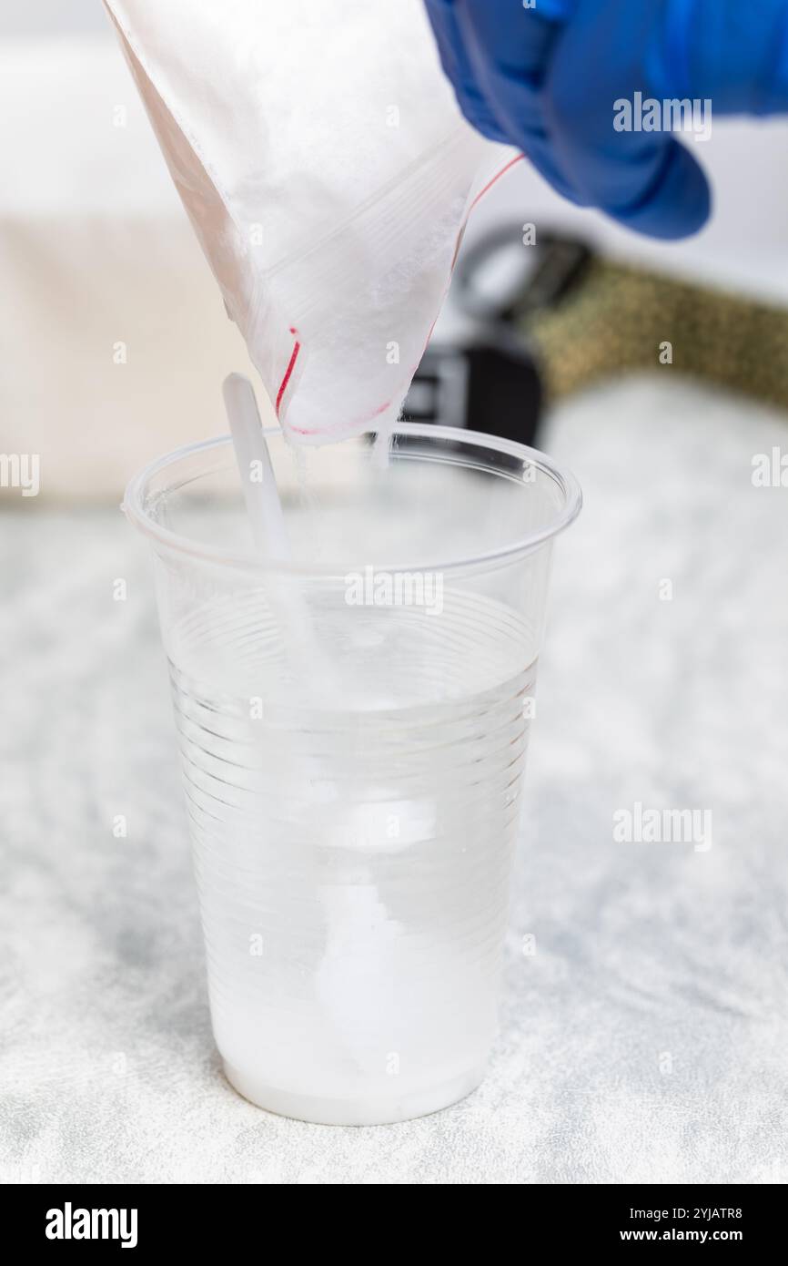 Gloved hands pouring glucose monohydrate powder into a plastic cup with ...