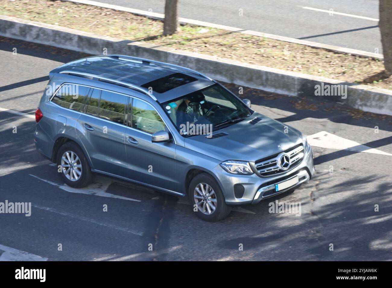 Silver mercedes benz gls driving on a paved road with trees on the side ...