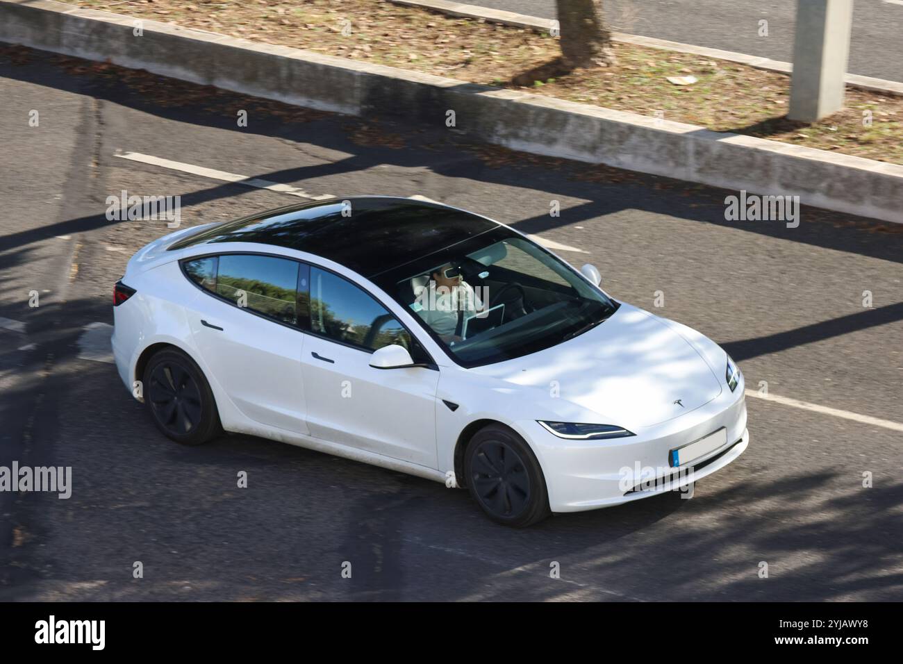 Businessman is driving a tesla model 3 electric car on the road ...