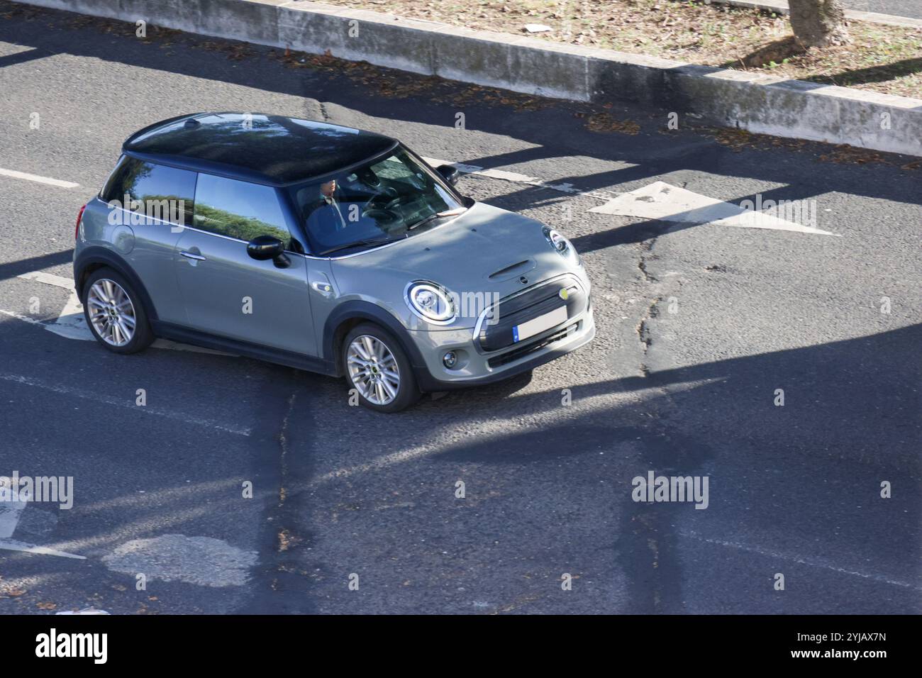 Modern grey mini cooper with a black roof driving down an asphalt road ...