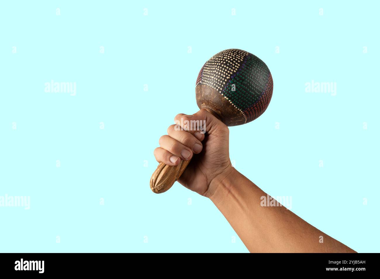 Male hand holding an ethnic design maraca isolated on light cyan ...