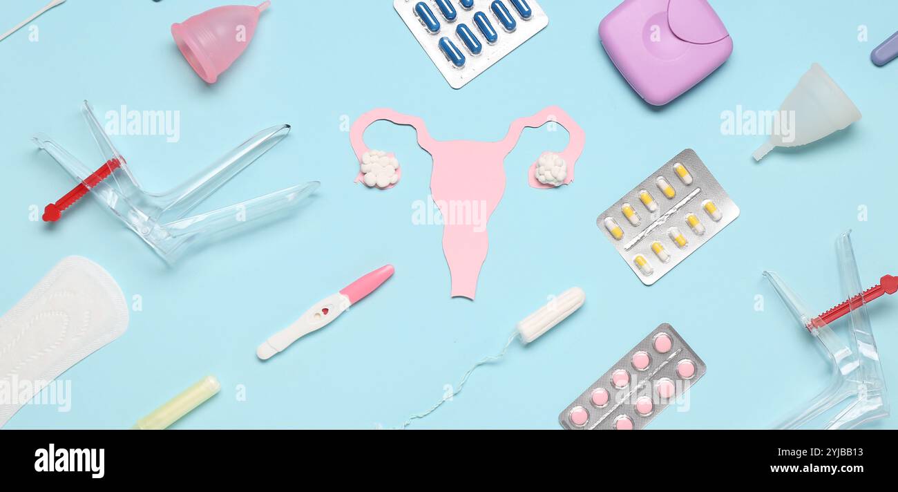 Paper uterus with gynecological supplies and pills on blue background ...
