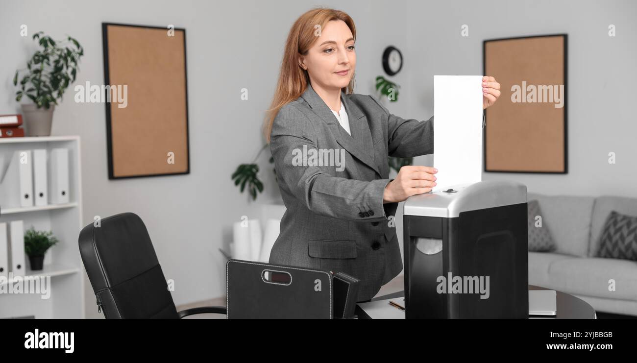 Mature secretary destroying documents by using shredder in office Stock ...