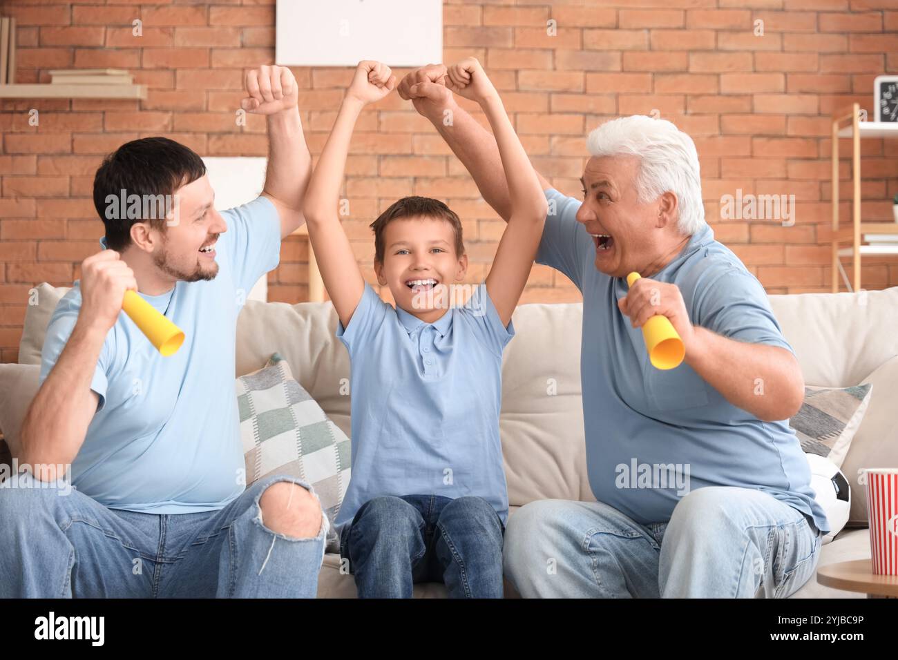 Boy with his dad and grandfather cheering for football team at home ...