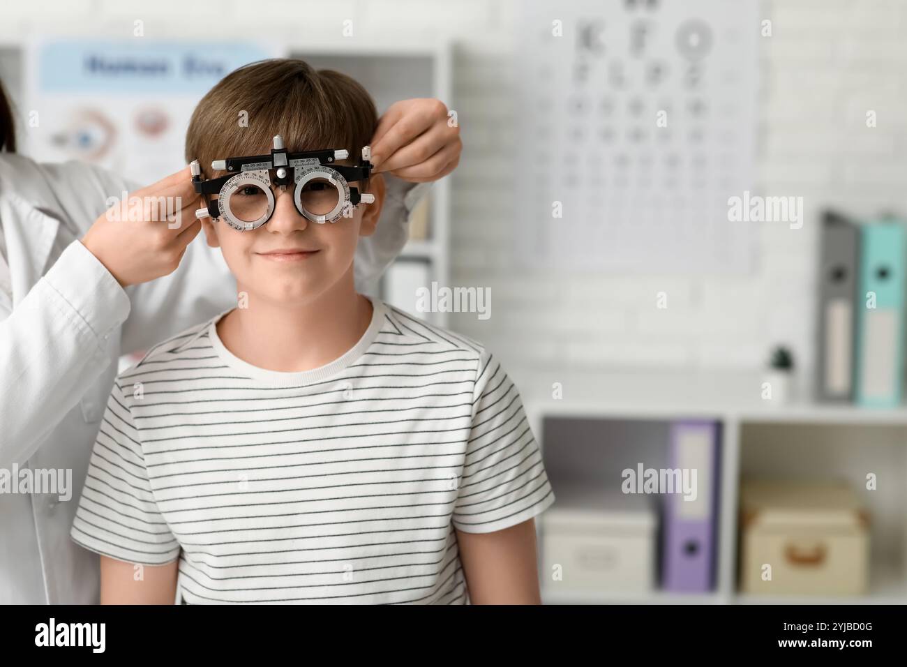 Female ophthalmologist helping little boy undergoing eye test in clinic ...