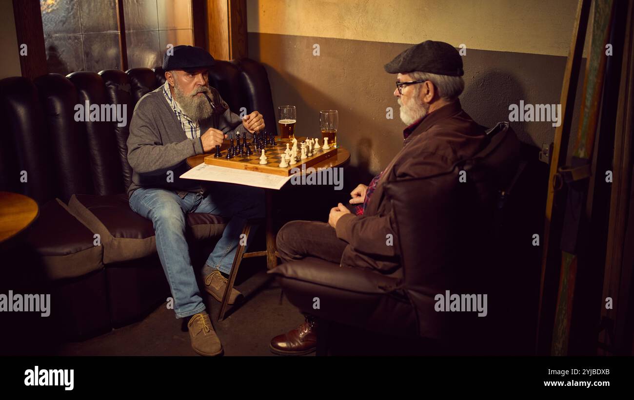 Two elderly bearded men in caps, sitting in cozy bar at wooden table ...