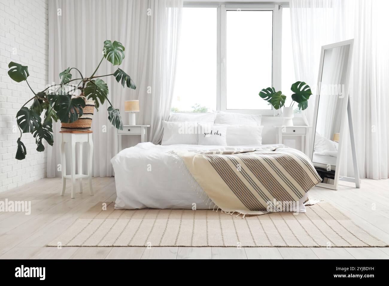 Interior of light bedroom with cozy bed and monstera leaves Stock Photo ...