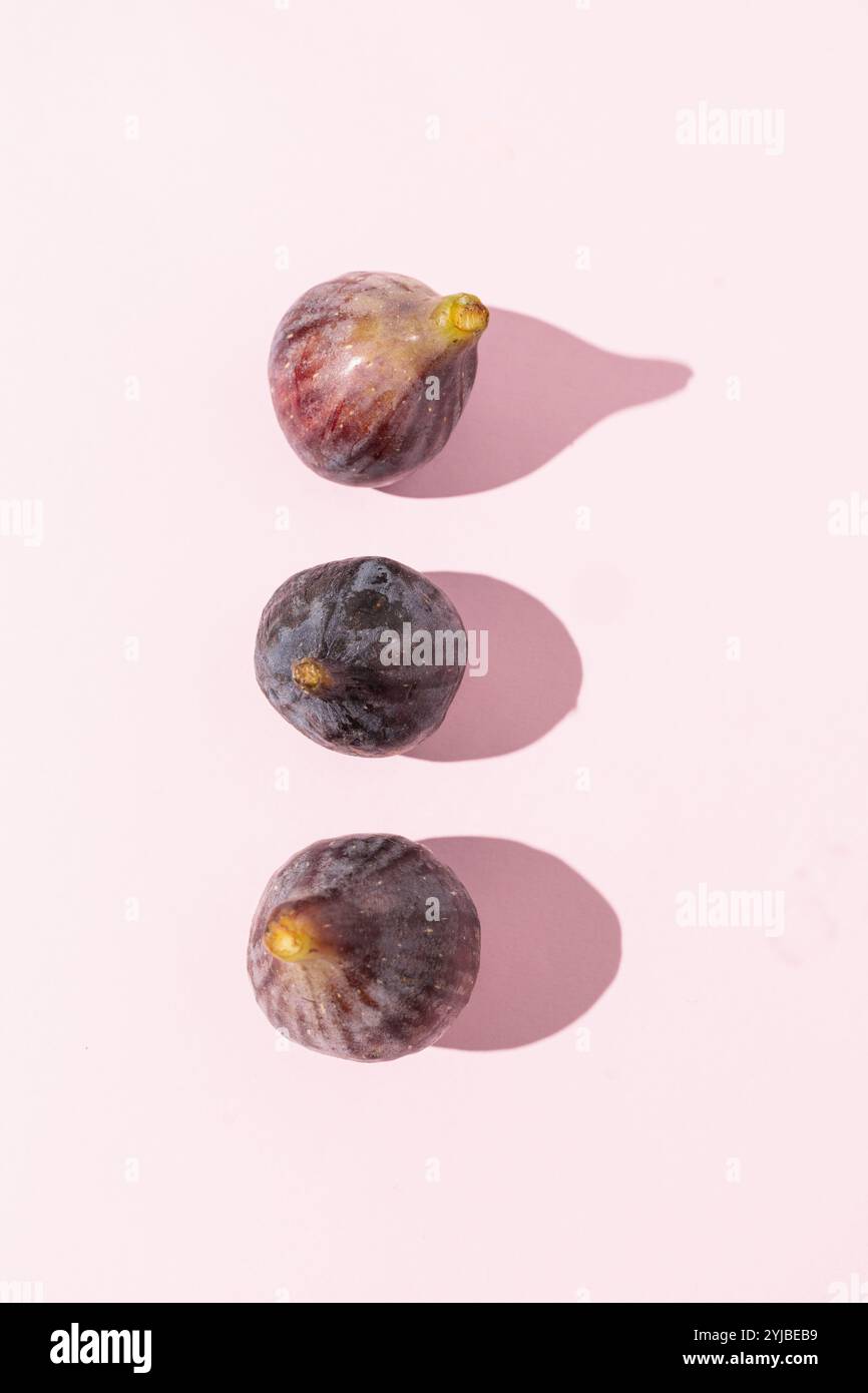 Top view of three ripe figs arranged on a soft pink background ...