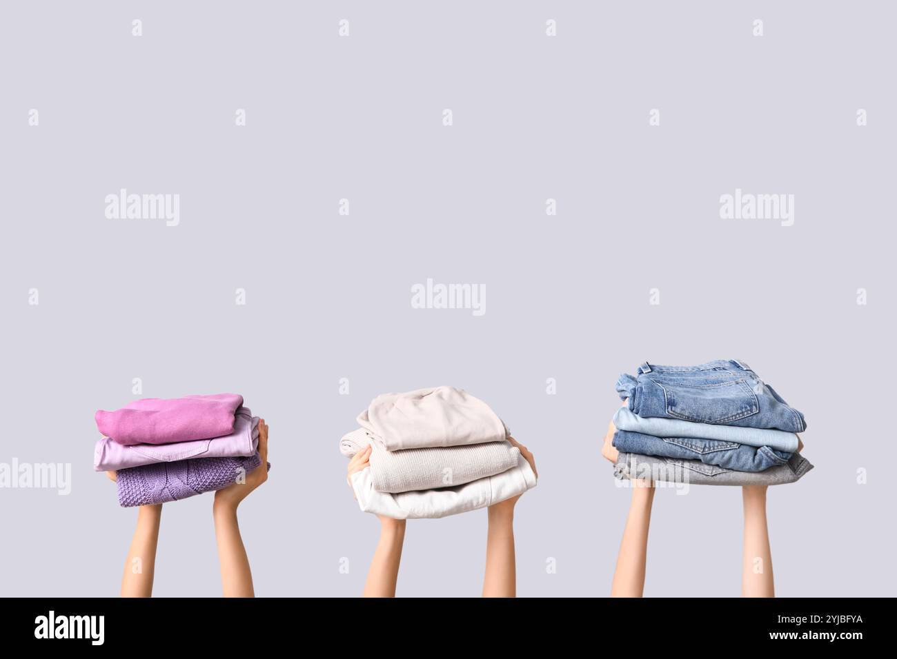 Many female hands with stacks of different clothes on grey background ...
