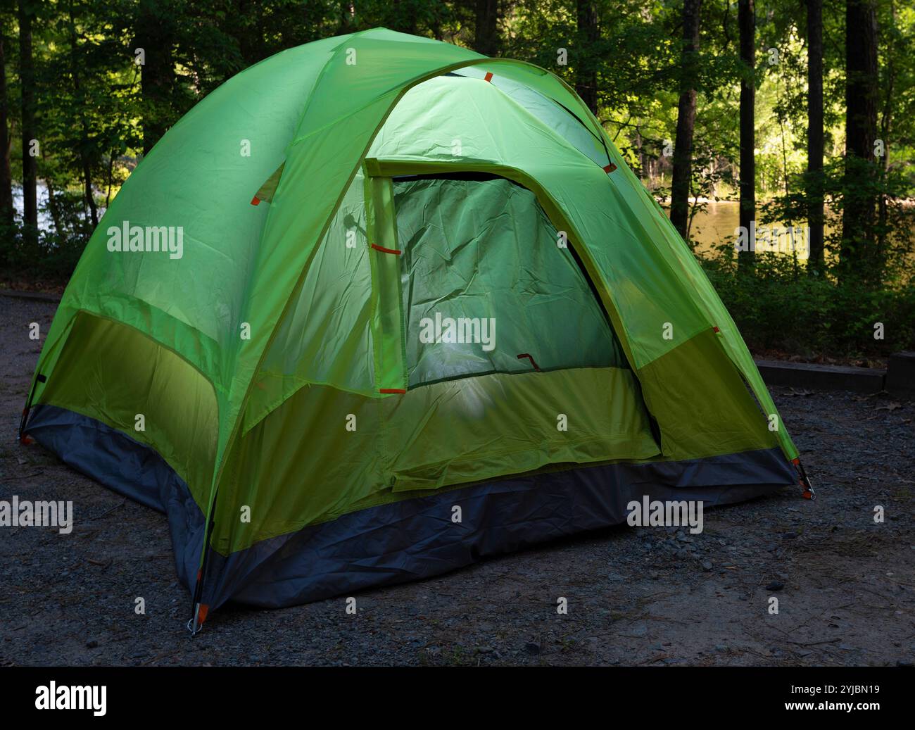 Small camping tent lighted within in a forest with lake bathed in ...