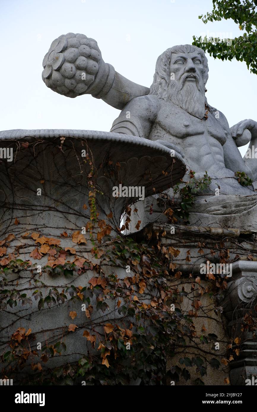 A stone statue of a muscular bearded man holding a club, with autumn ...