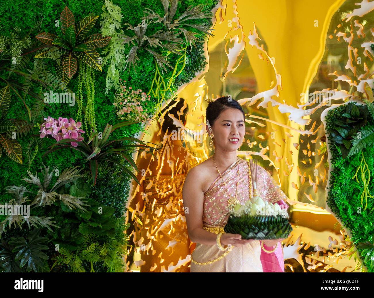 A tourist dressed in traditional Thai attire holds a krathong and poses ...