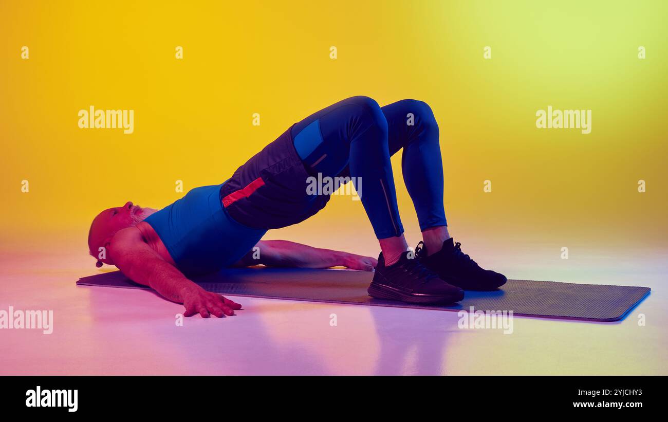 Senor man in sportswear lying on fitness mat and doing glute bridge ...
