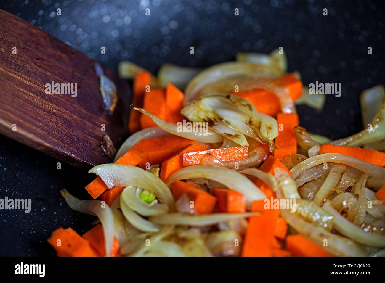 cooking frying half rings of onion with pieces of fresh carrot in a ...